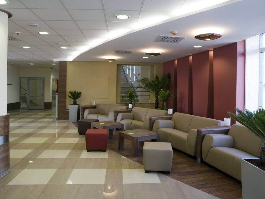 Um hall moderno com piso xadrez, sofás de couro e uma escada ao fundo.