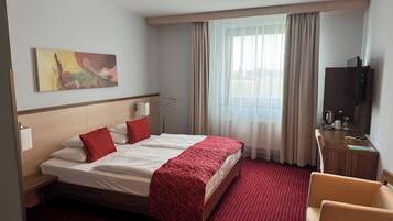 Quarto de hotel com uma cama grande, uma escrivaninha com cadeira, televisão e janela com cortinas.