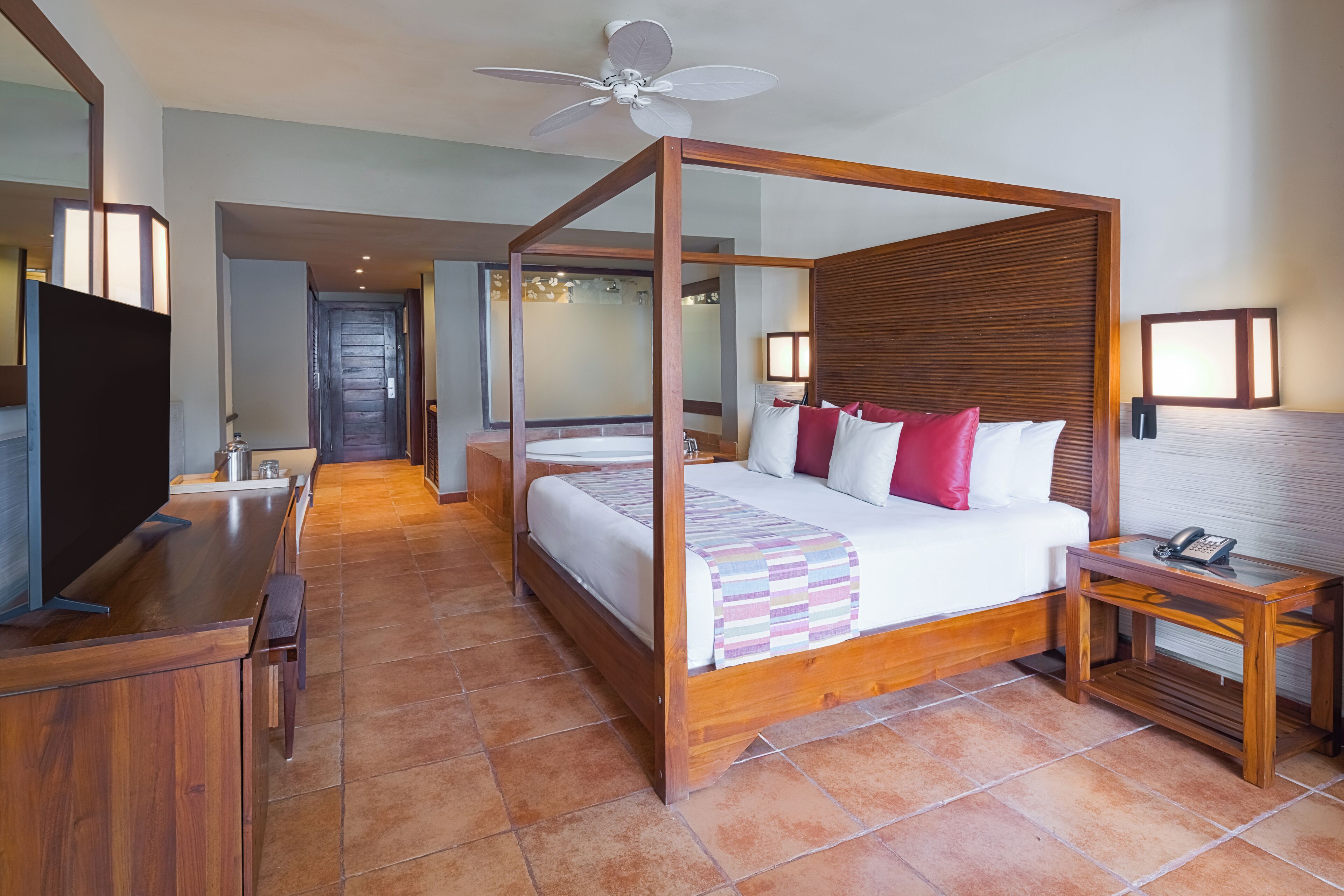 Um quarto de hotel espaçoso com cama de dossel, escrivaninha de madeira, televisão e mesa de cabeceira separada.