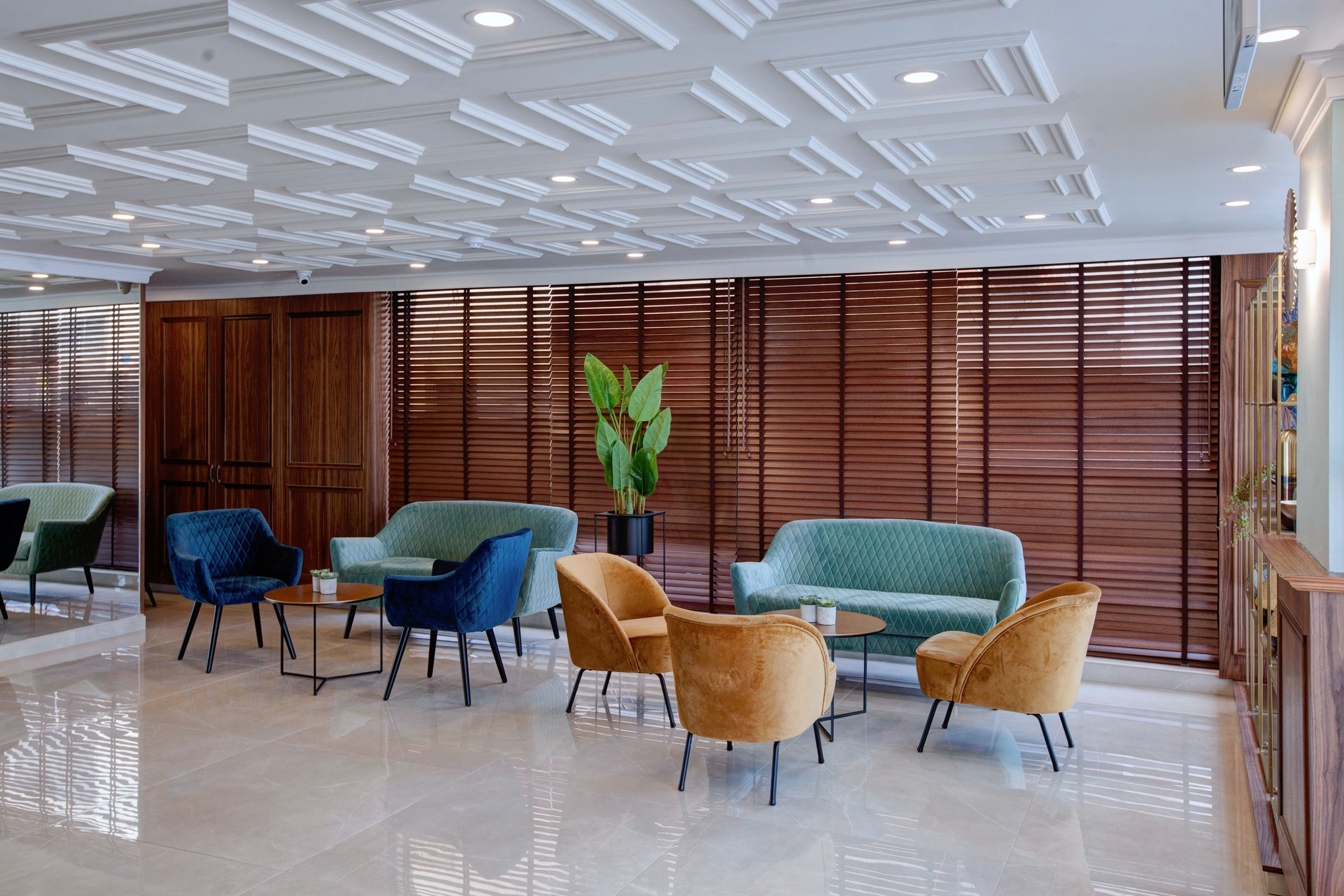 Um lobby moderno com design geométrico no teto, painéis de madeira nas paredes e diversas opções de assentos, incluindo poltronas e sofás.