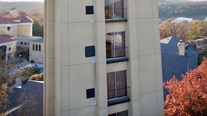Um edifício alto com vários andares e varandas, cercado por árvores e outros edifícios.