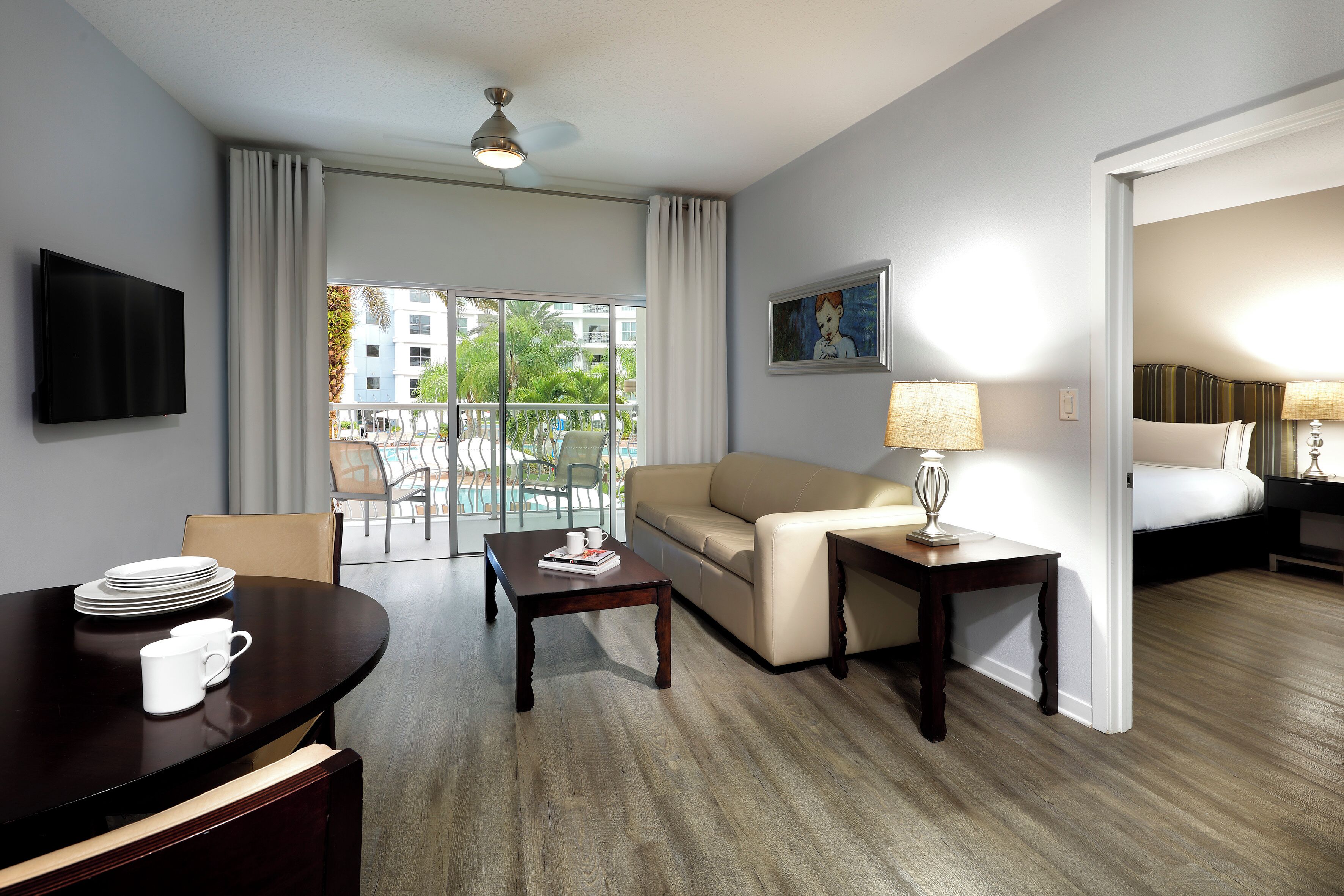 Quarto de hotel com varanda, sofá, cama, televisão e mesa de jantar com cadeiras.