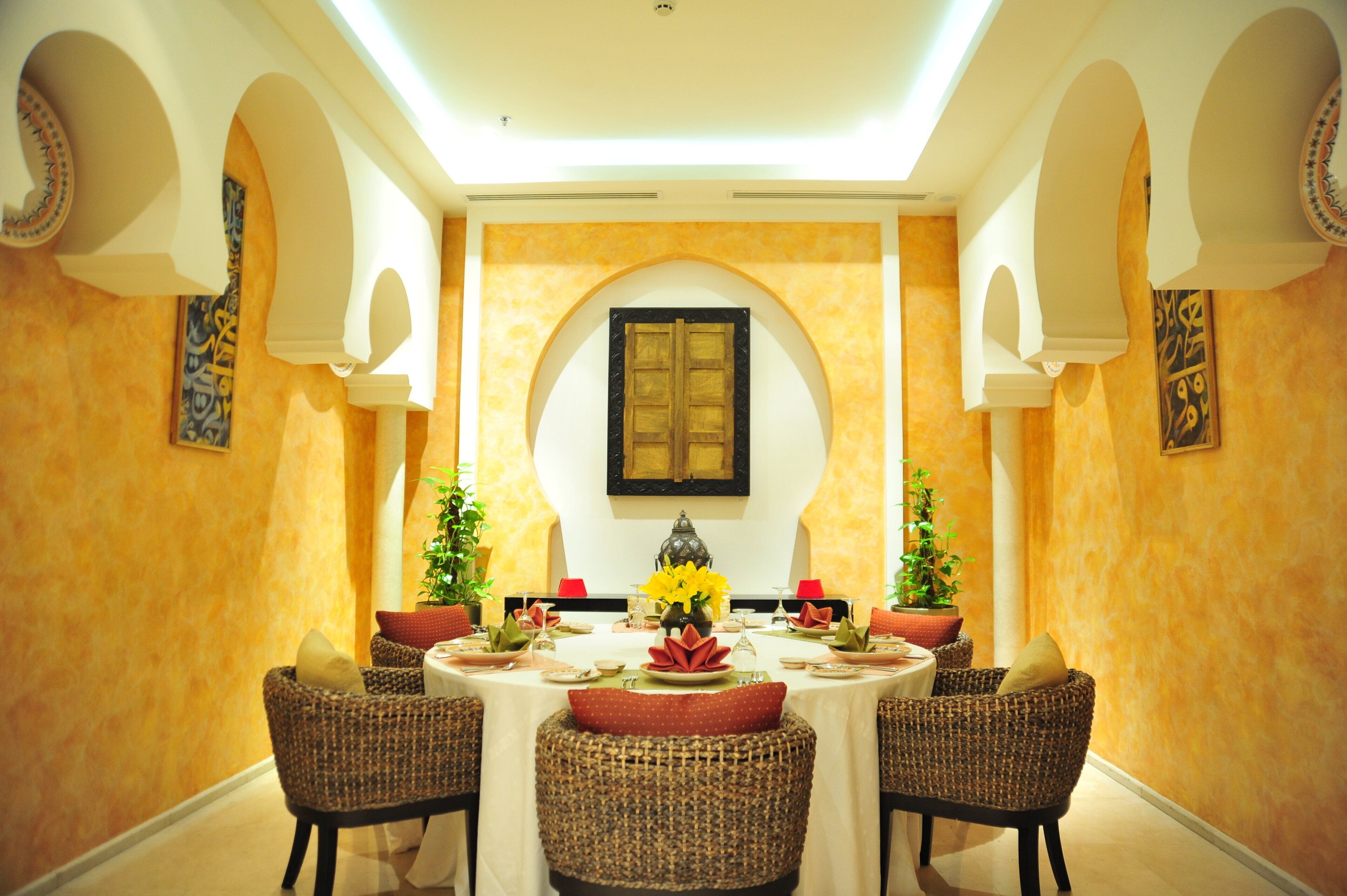 Sala de jantar com mesa redonda, quatro cadeiras de vime e um objeto decorativo central.