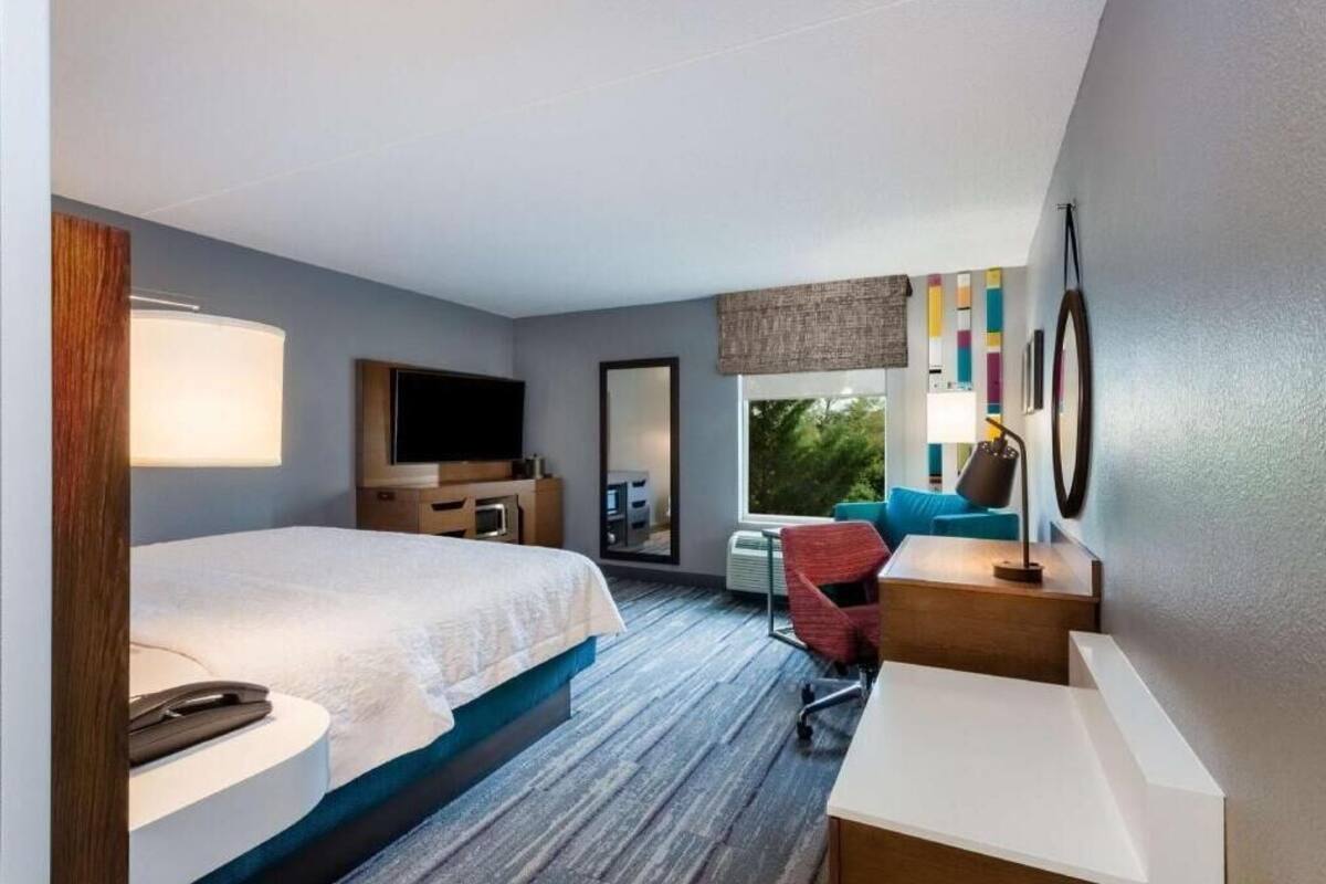 Quarto de hotel com cama, escrivaninha, cadeira, TV e vista para o exterior.