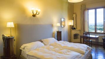 Quarto de hotel com cama, luminárias de cabeceira, escrivaninha e vista para o exterior.