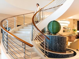 Interior moderno com escadaria em espiral, um globo decorativo e uma área de recepção com mobiliário.