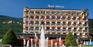 Um hotel com várias varandas, uma fonte e uma placa com a inscrição 'Hotel Astoria'.