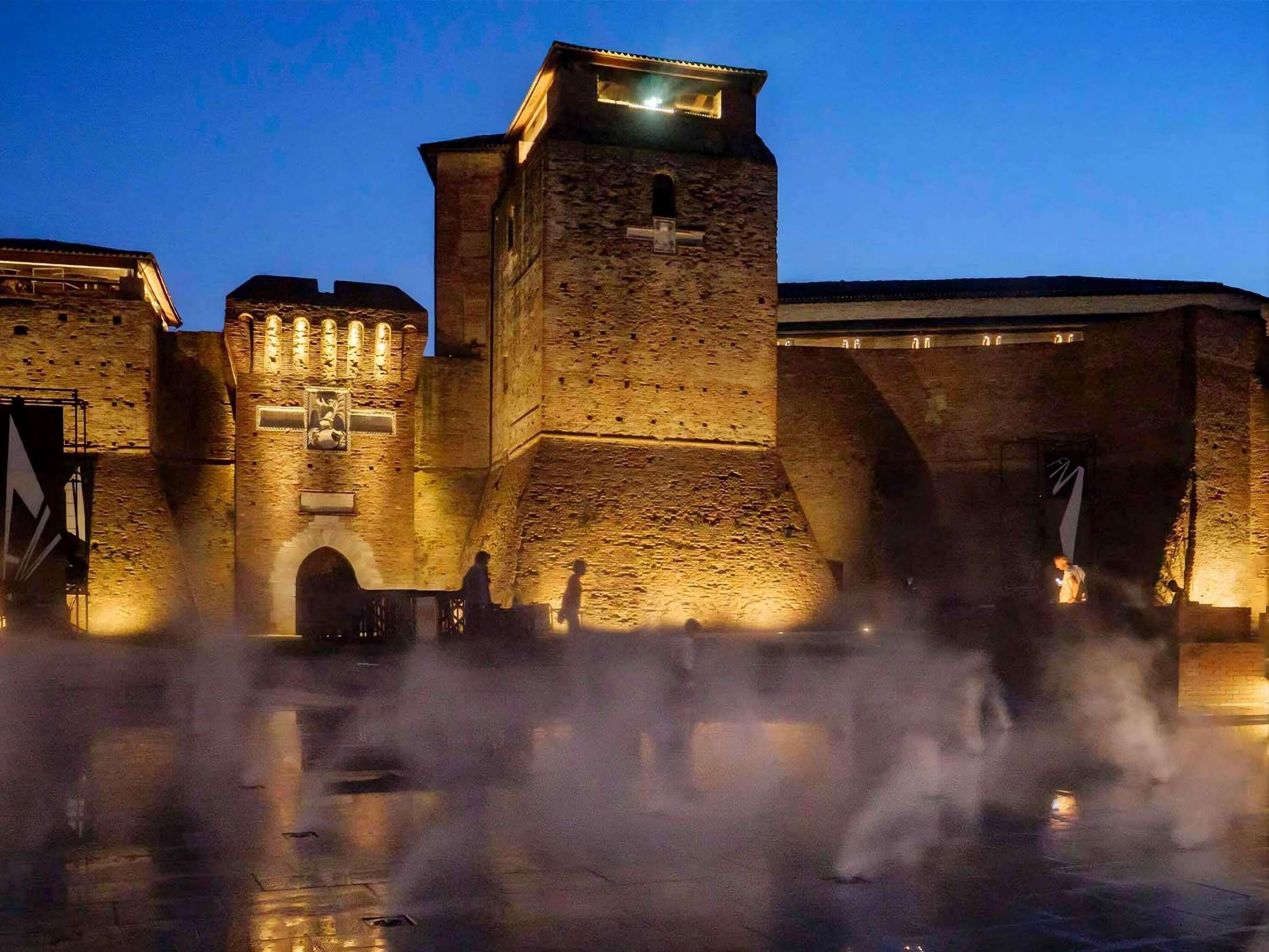 Um edifício histórico com uma torre imponente e estruturas em arco, iluminado por iluminação artificial.