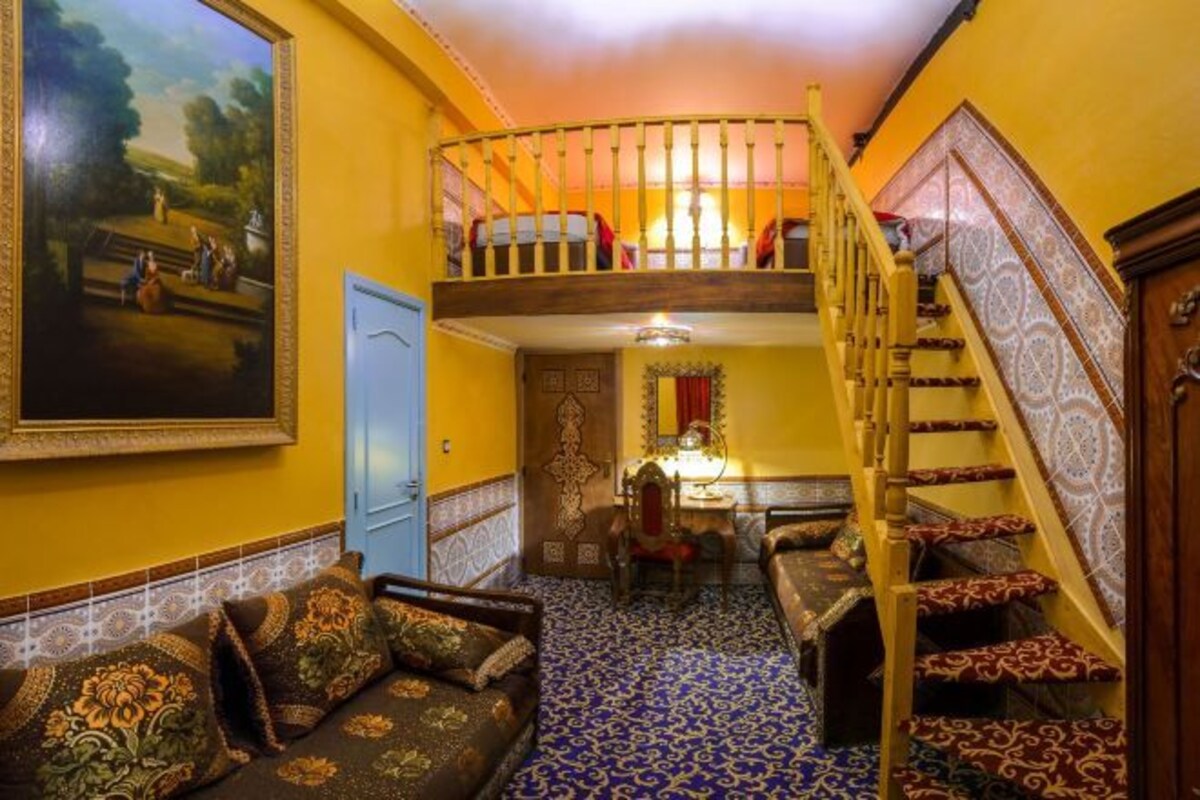 Quarto com teto alto, varanda, escada, sofá, mesa e um quadro.