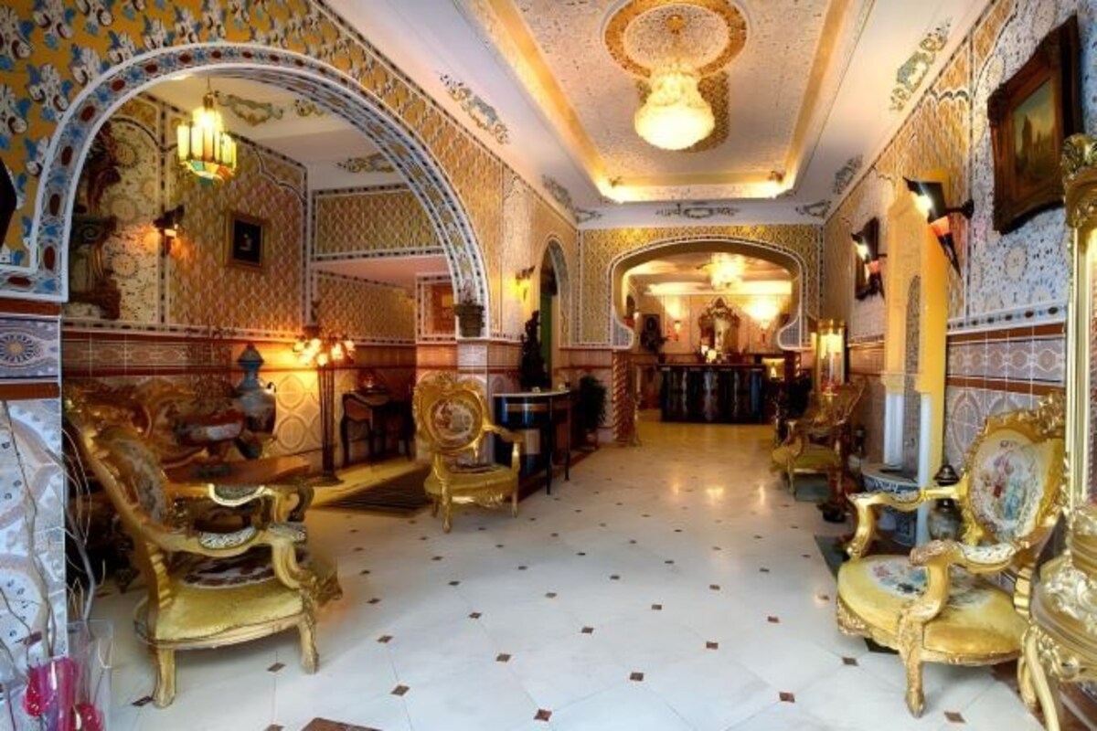 Um interior ornamentado com mobiliário emoldurado a ouro, paredes estampadas e um lustre.