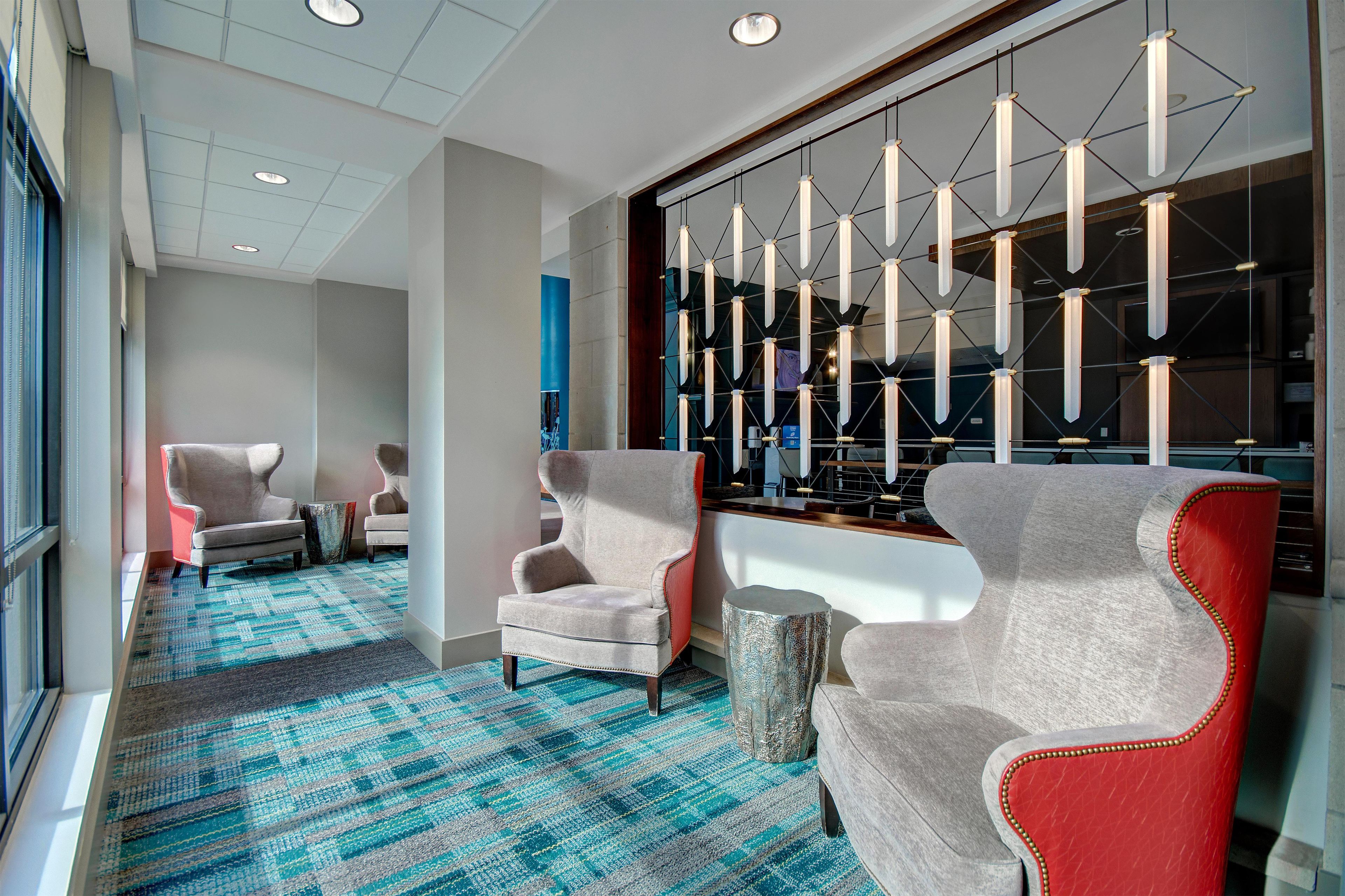 Um saguão de hotel com design moderno, apresentando um carpete estampado, área de estar com poltronas e uma luminária única.