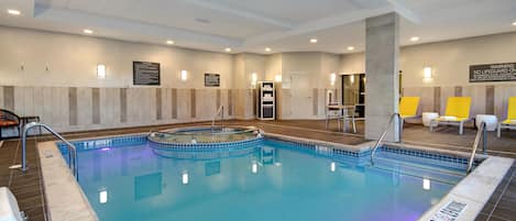 Piscina interior com água cristalina, bordas azulejadas e escada para piscina. Há cadeiras de descanso e um aviso com as regras da piscina.