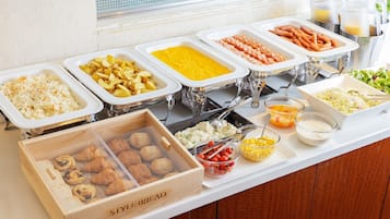 Buffet com diversos alimentos, incluindo arroz, batatas, salsichas e pão.