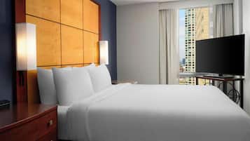 Quarto de hotel com uma cama grande, cabeceira de madeira, televisão e janela com vista para a cidade.