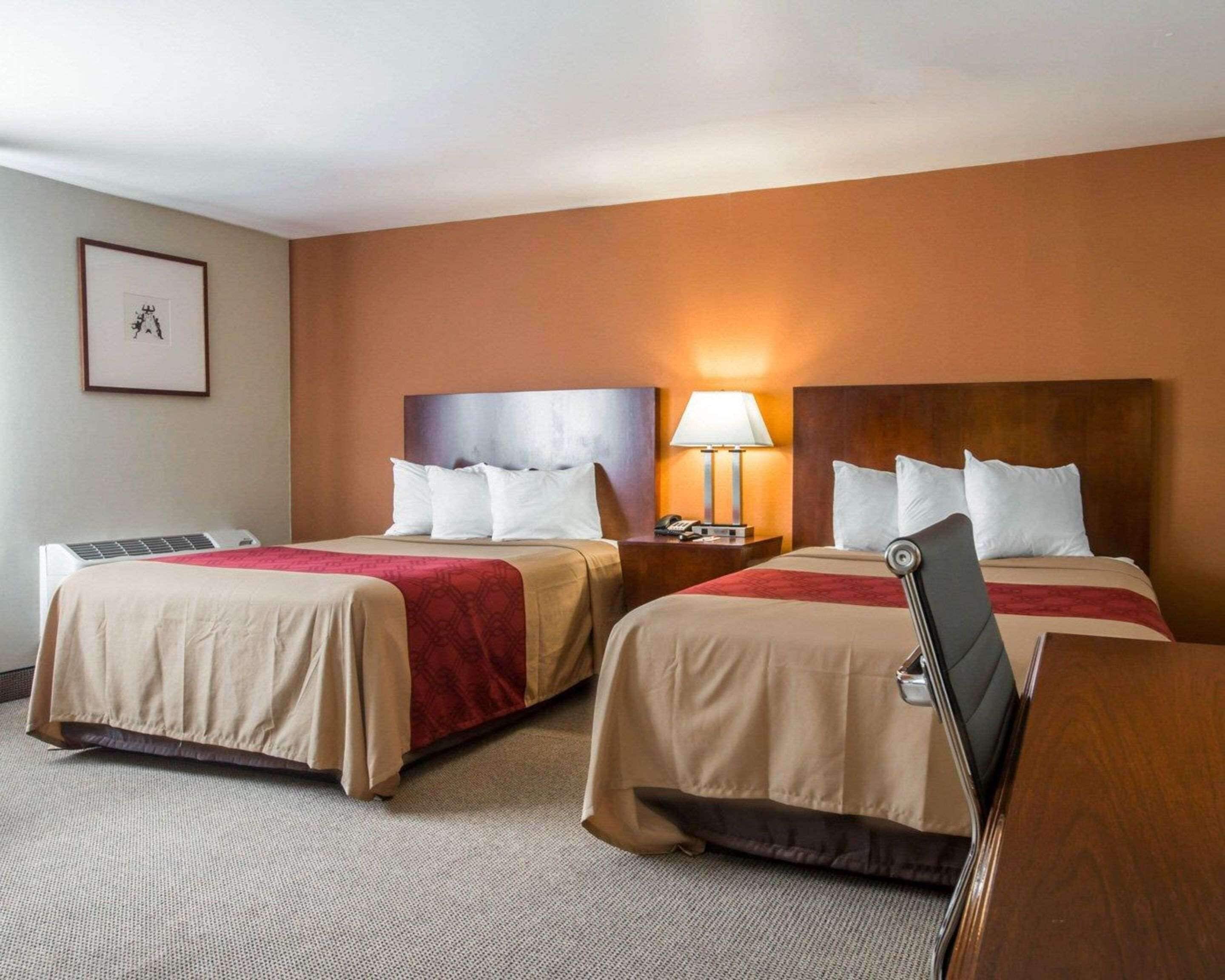 Quarto de hotel com duas camas, uma mesa de cabeceira com abajur e um quadro na parede.