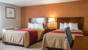 Quarto de hotel com duas camas, uma mesa de cabeceira com abajur e um quadro na parede.