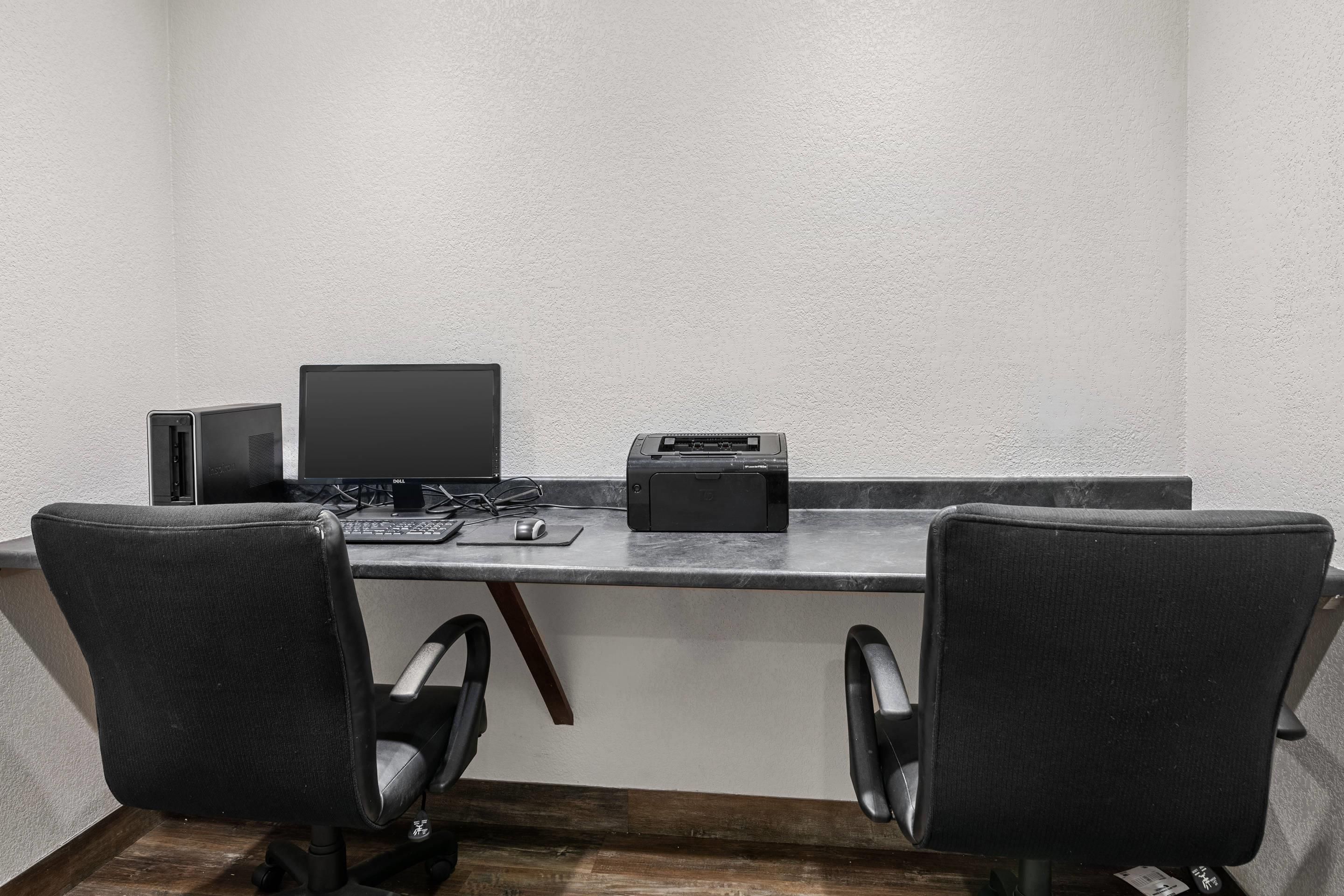 Um pequeno escritório com uma mesa, duas cadeiras, um computador e uma impressora.