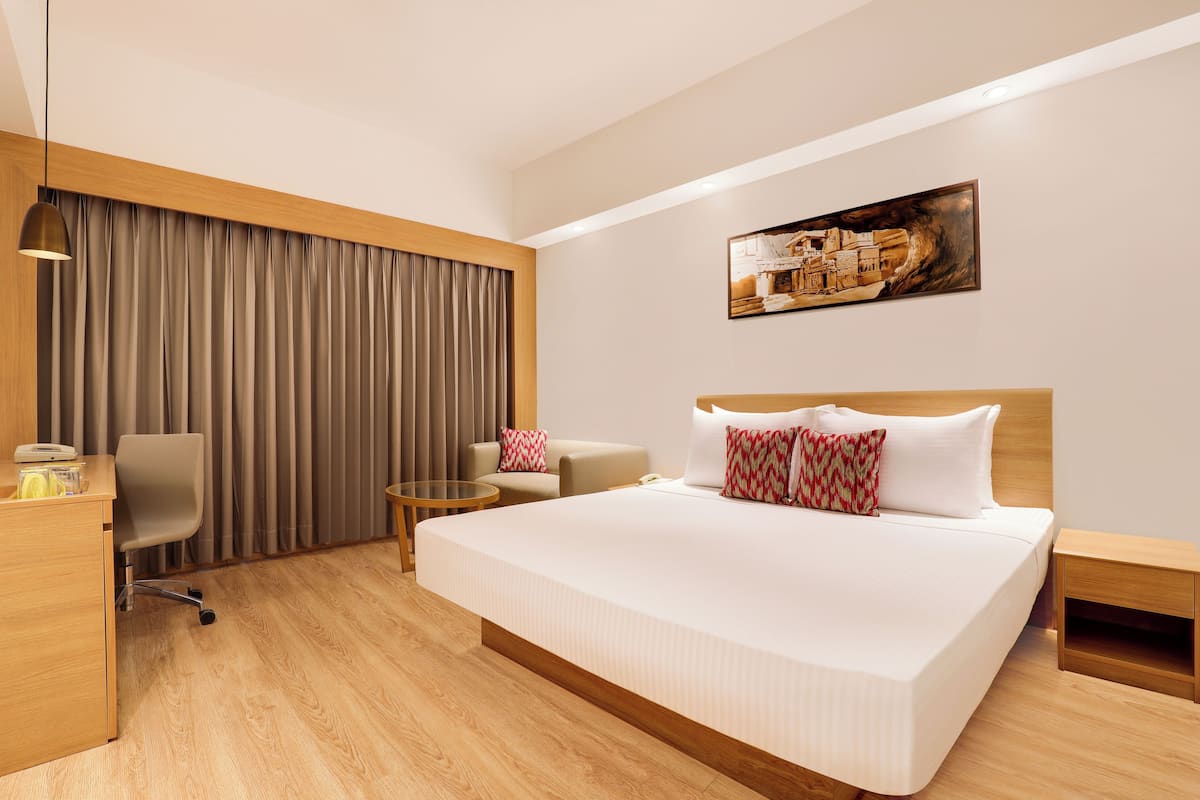 Quarto de hotel com uma cama grande, uma escrivaninha, uma cadeira, uma mesinha e um quadro na parede.