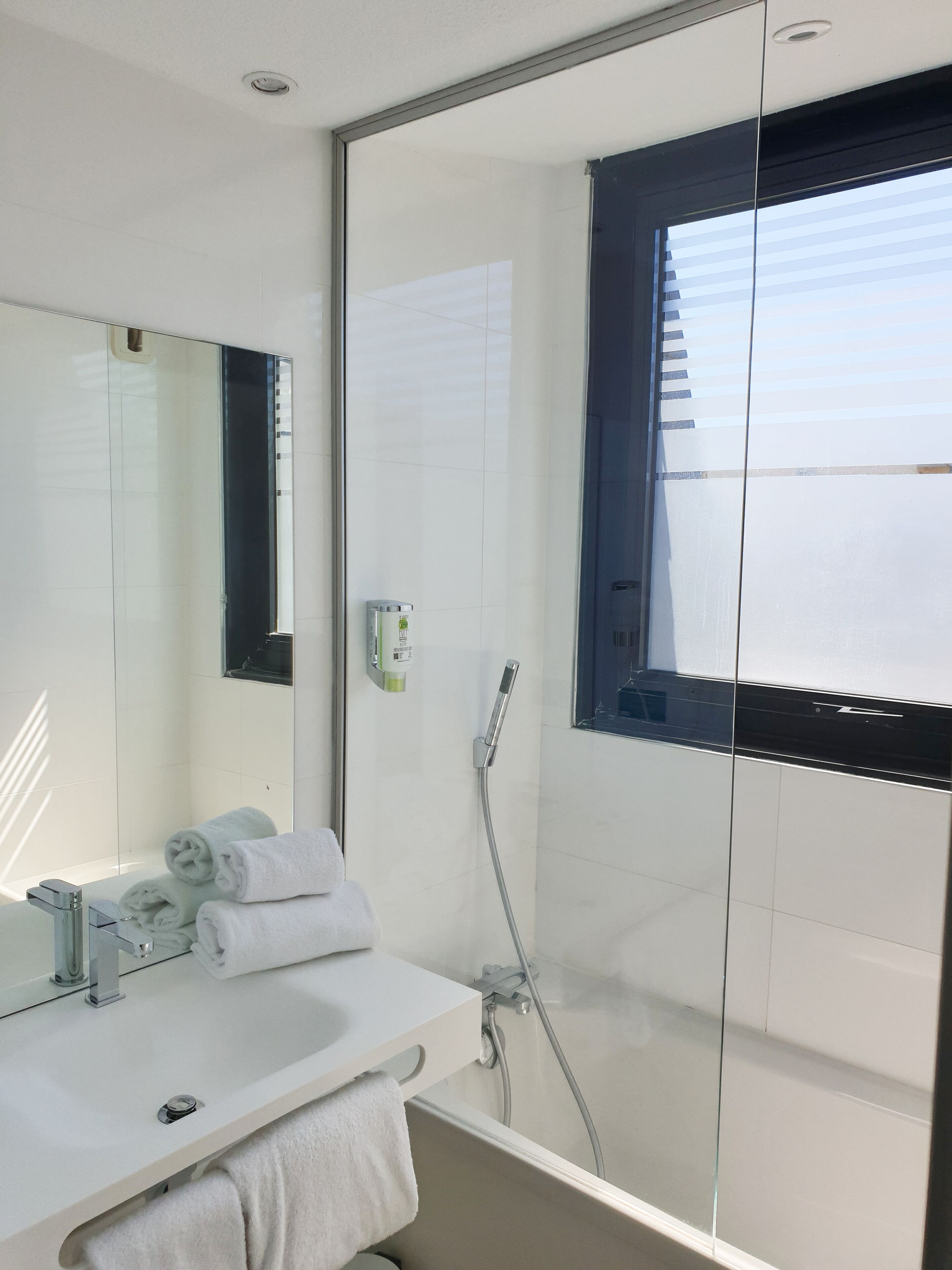 Casa de banho moderna com cabine de duche em vidro, lavatório branco e espelho.