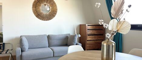 Uma sala de estar moderna com um sofá cinzento, uma mesa de madeira redonda e um vaso decorativo com flores secas.