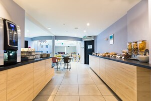 Uma cozinha de hotel moderna com um balcão comprido, uma máquina de café e um espaço para refeições com diversas opções de comida.