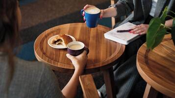 Uma mesa de madeira com uma chávena de café, um pastel, um caderno e uma caneta.