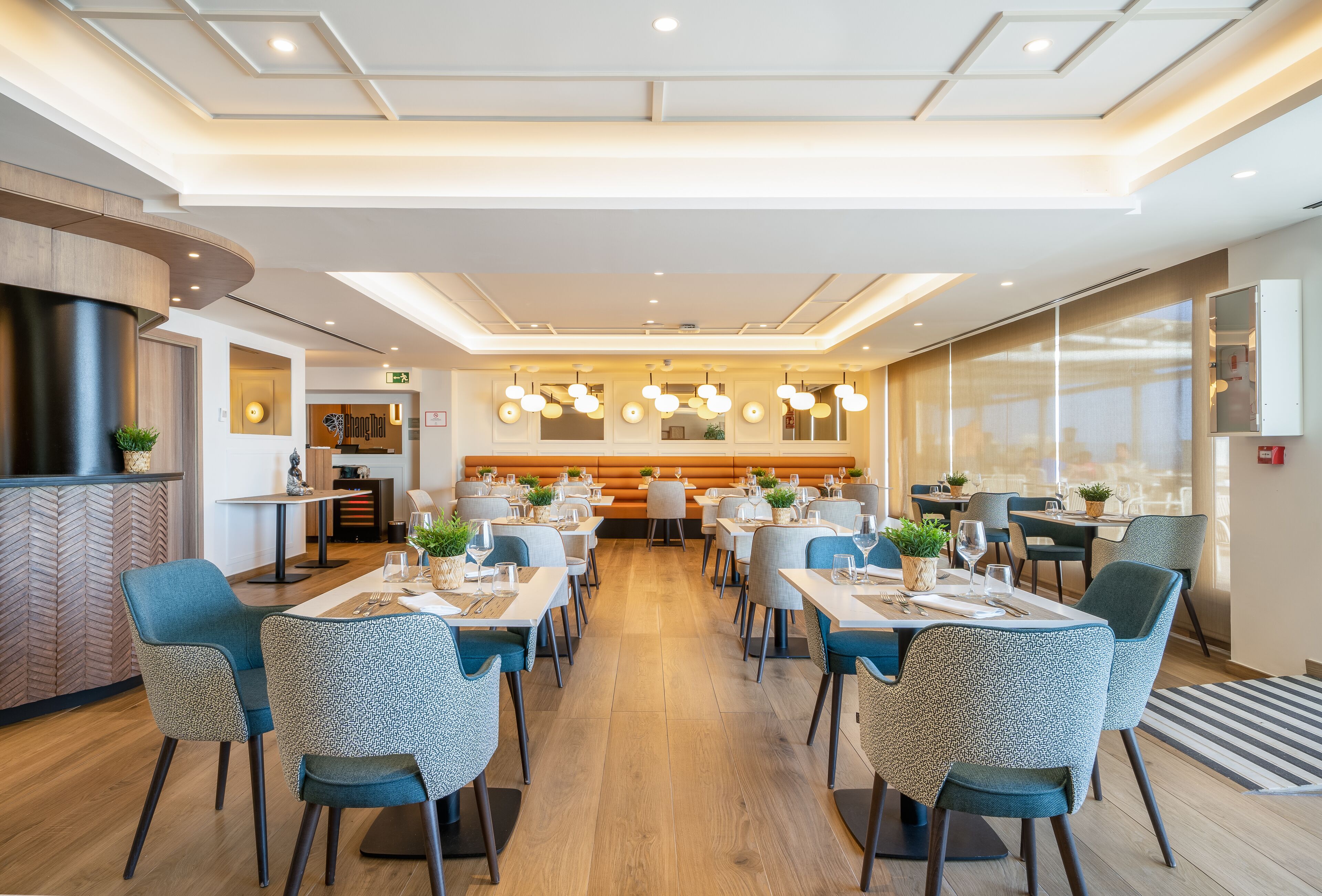 Um restaurante moderno com uma área de estar central, mesas individuais e diversos tipos de cadeiras.