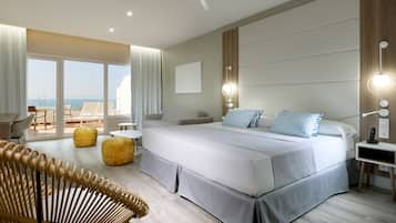 Quarto de hotel moderno com uma cama grande, área de estar com cadeiras e vista para o mar.