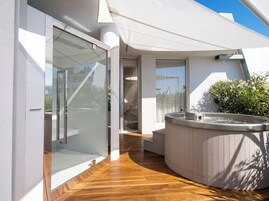 Um espaço exterior moderno com deck de madeira, banheira de hidromassagem e porta de vidro que dá para um quarto.