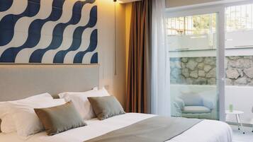 Quarto de hotel com uma cama grande, cabeceira moderna, porta de vidro para uma varanda e parede de pedra.