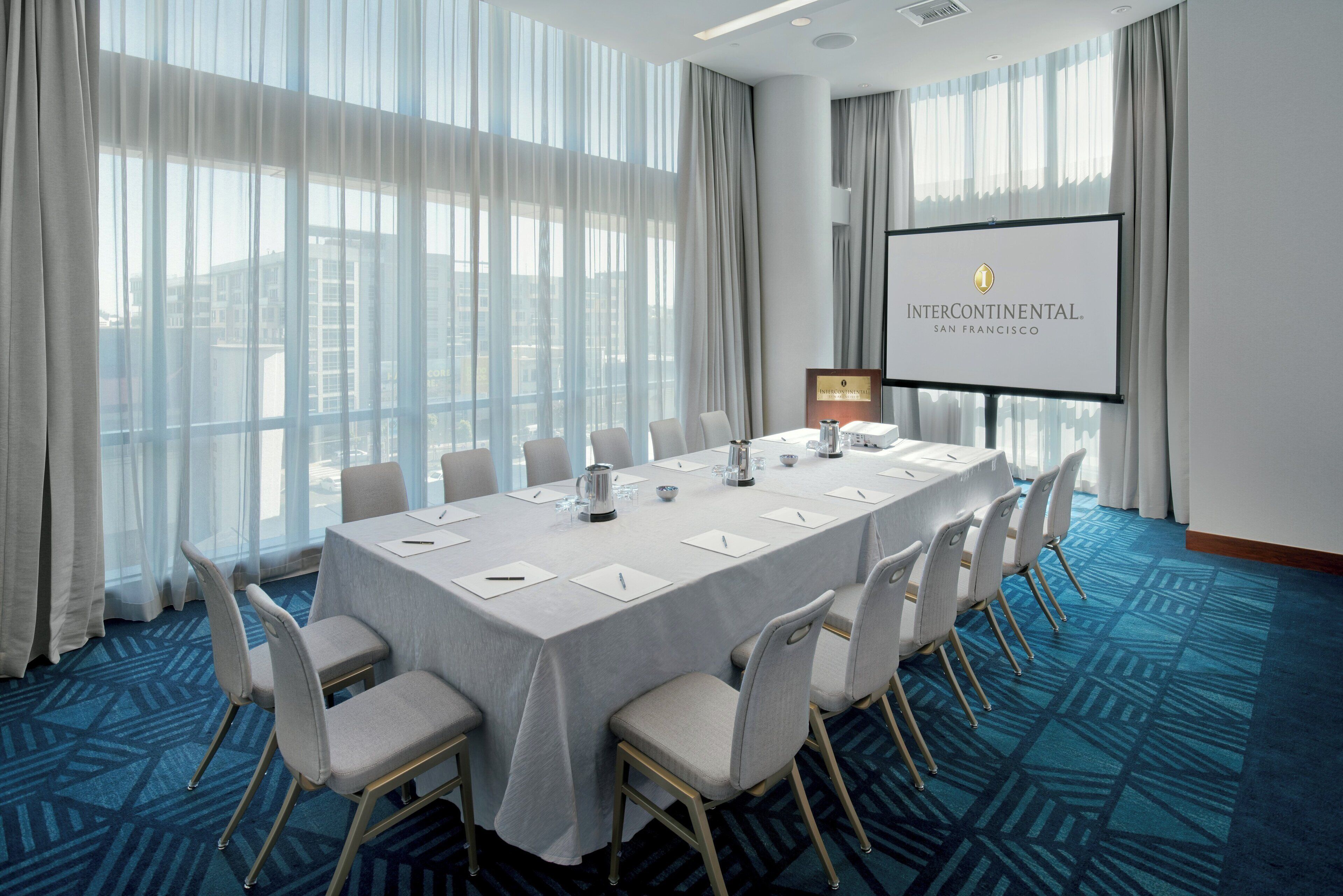 Sala de conferências com uma mesa comprida, cadeiras e uma tela de projetor exibindo o logotipo do InterContinental San Francisco.