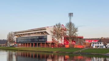 Um estádio moderno com fachada de vidro, esquema de cores vermelho e branco, e reflexo na água em frente.