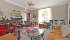 Sala de estar com lareira, móveis em vermelho e marrom, uma mesa de centro de vidro e um candelabro.