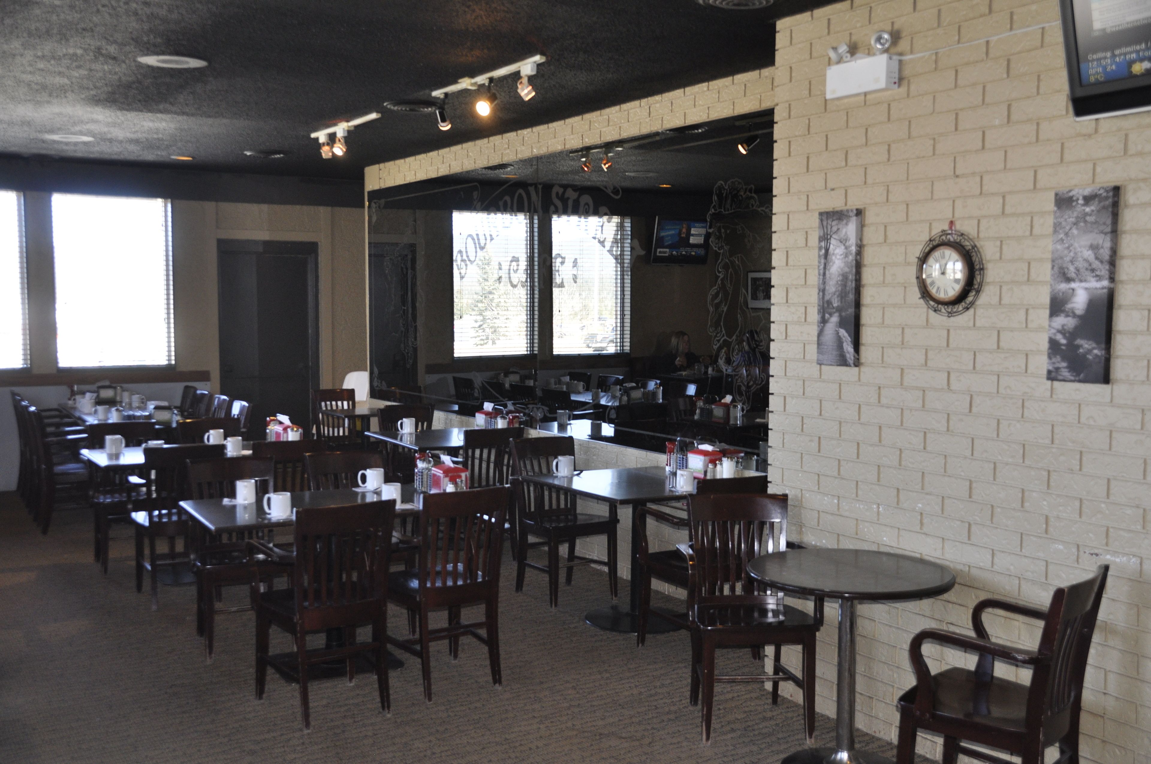 Restaurante com várias mesas, cadeiras, área de bar e grandes janelas que permitem entrada de luz natural.