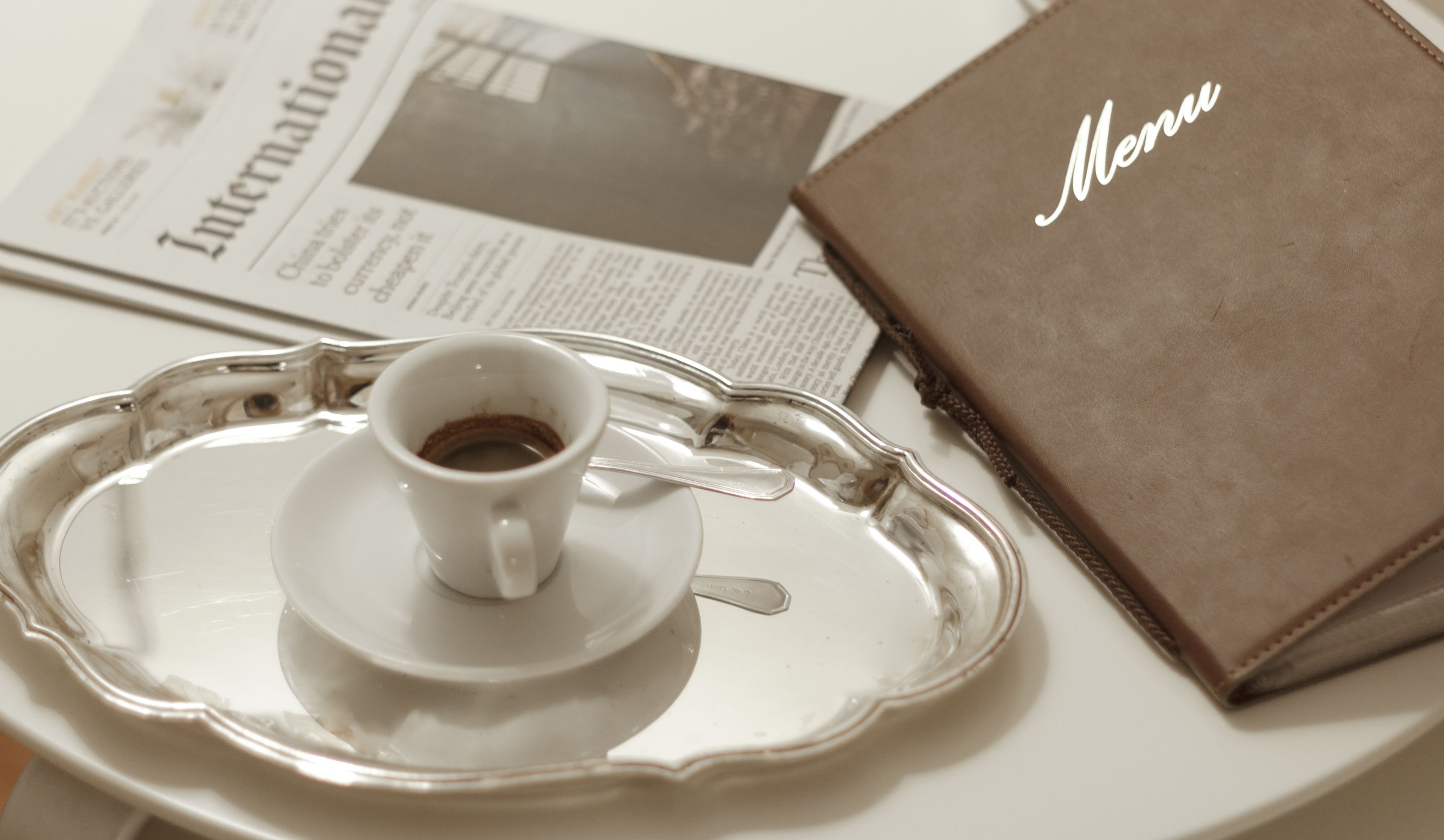 Uma chávena de café, um menu e um jornal sobre uma mesa.