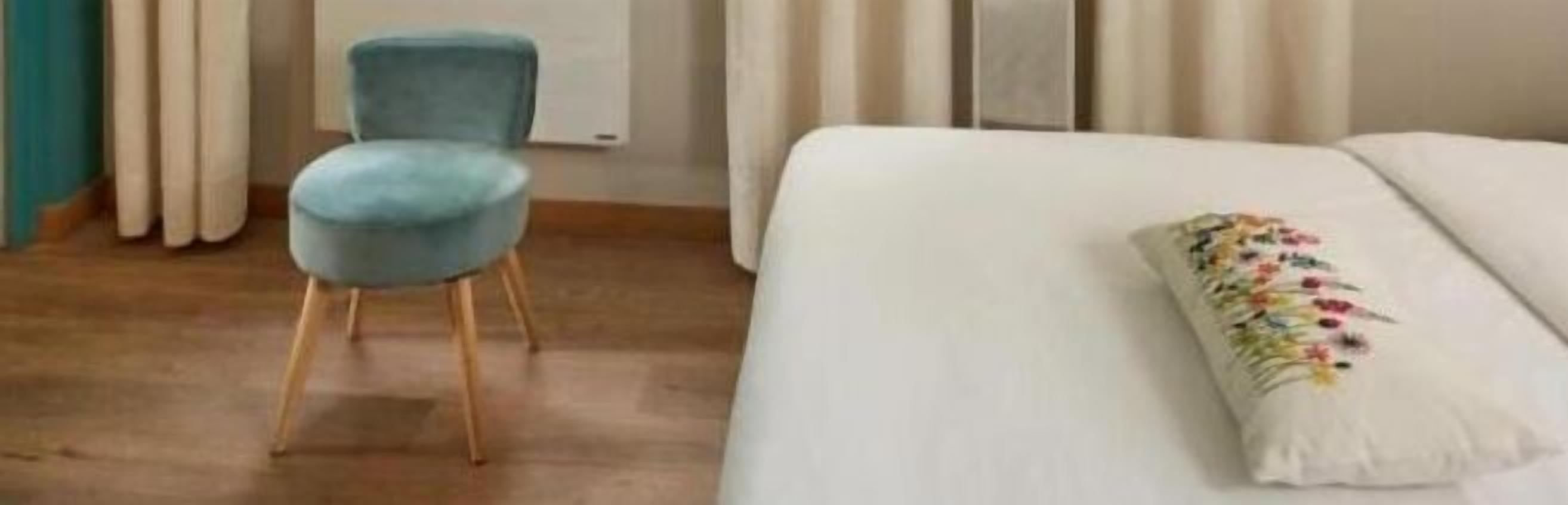 Um quarto com uma cama, uma cadeira azul e uma janela com cortinas.