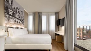 Quarto de hotel moderno com uma cama grande, uma mesa de escritório, televisão de tela plana e varanda com vista para a cidade.