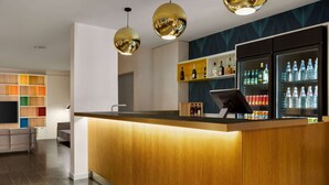 Uma área de recepção com balcão de madeira, uma máquina registradora e um refrigerador cheio de bebidas.