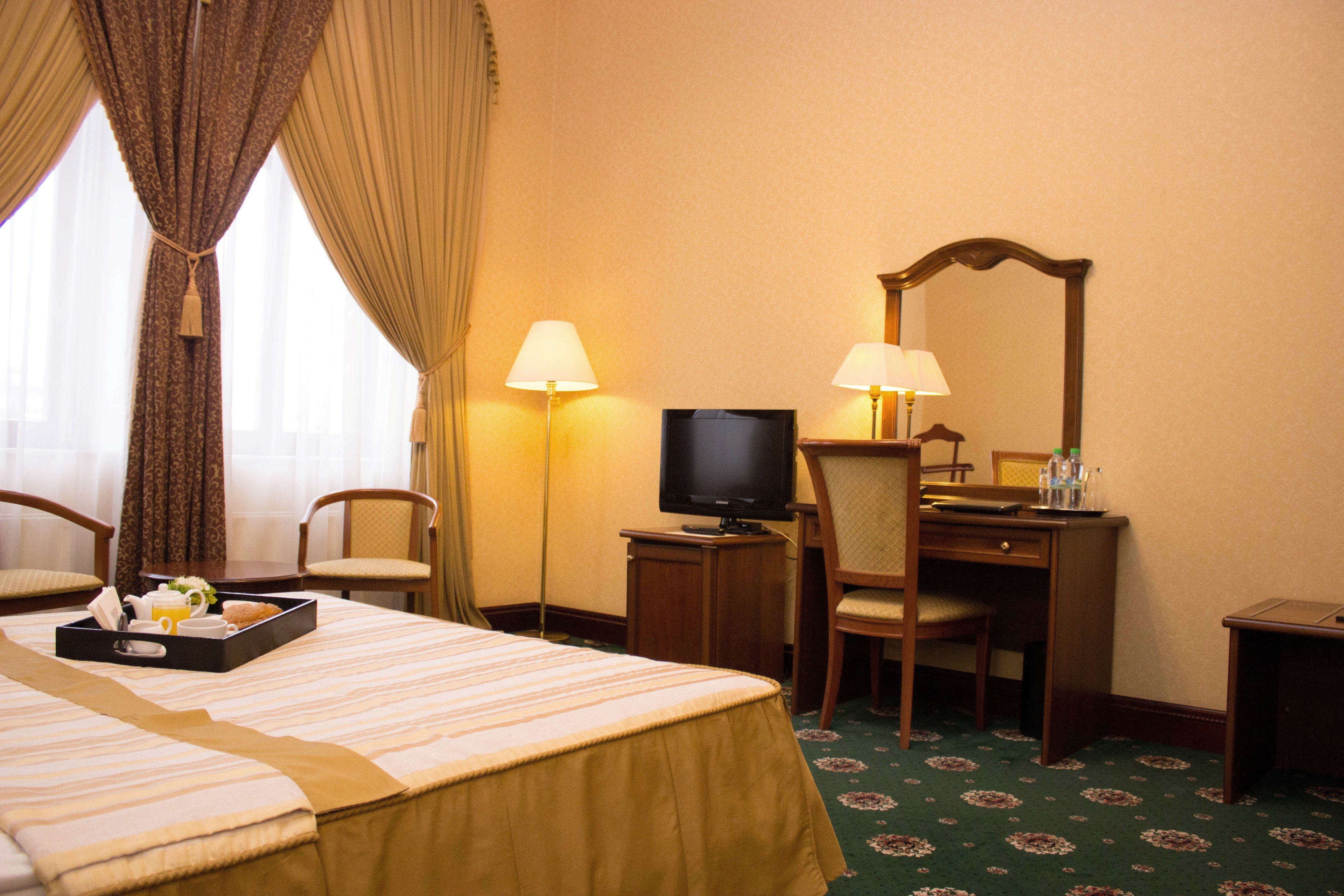 Quarto de hotel com cama, escrivaninha, cadeira, televisão e bandeja com itens de café da manhã.