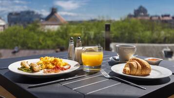 Uma mesa com itens de café da manhã, incluindo ovos mexidos, torradas e um croissant, além de um copo de suco de laranja e uma xícara de café.