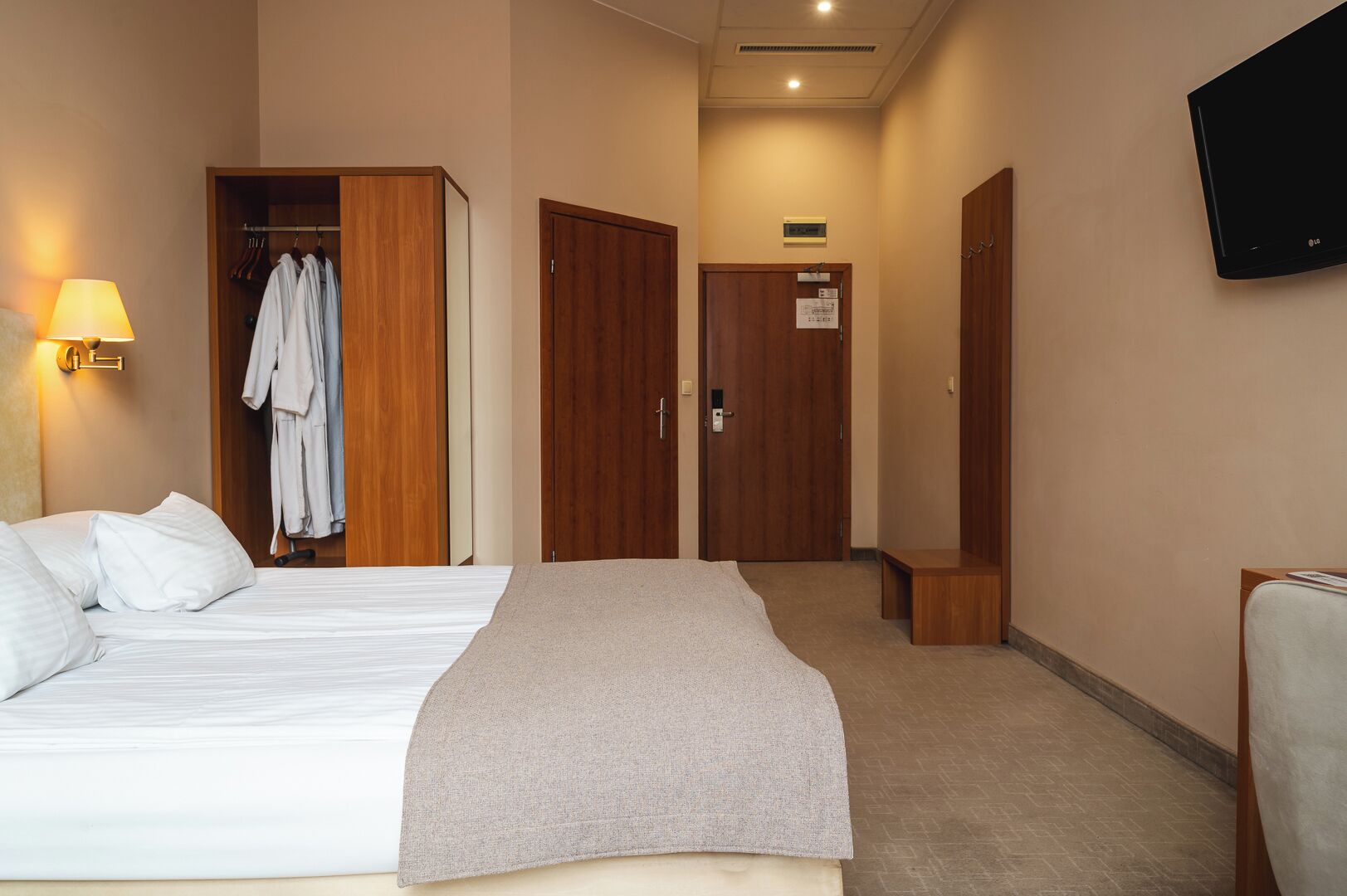 Quarto de hotel com cama, cabideiro, escrivaninha e televisão.
