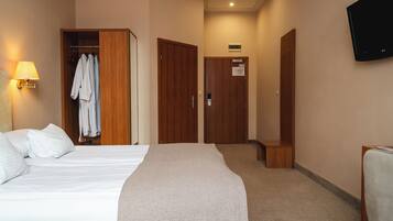 Quarto de hotel com cama, cabideiro, escrivaninha e televisão.