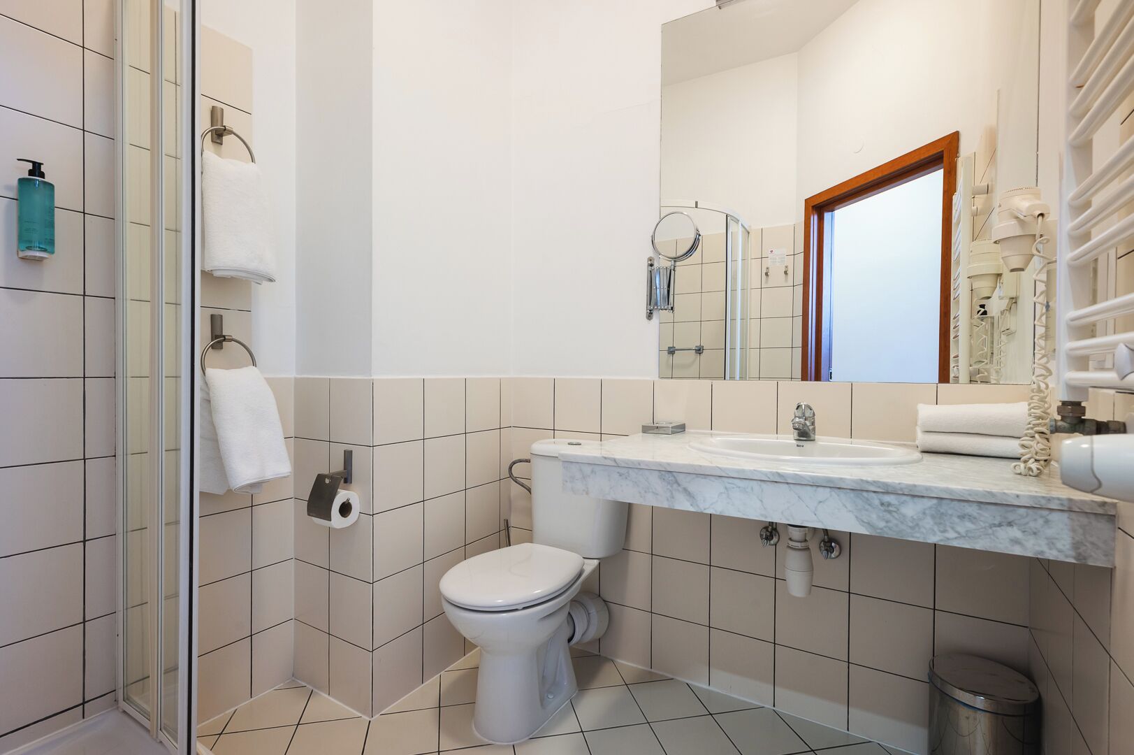 Um banheiro moderno com box de vidro, vaso sanitário branco, pia de mármore e espelho com moldura de madeira.