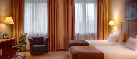 Quarto de hotel com duas camas, uma escrivaninha com cadeira e uma luminária.