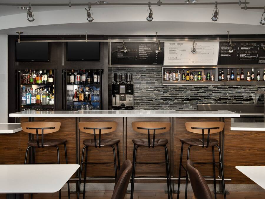 Uma área de bar moderna com um balcão comprido, banquetas e um quadro de cardápio.