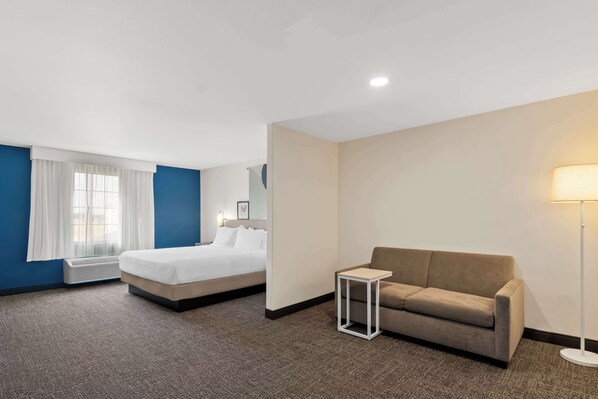 Quarto de hotel com cama, sofá, mesa pequena e luminária.