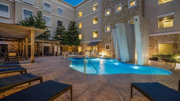 Uma área de piscina com espreguiçadeiras, um espaço de estar coberto e um edifício de pedra com várias janelas.