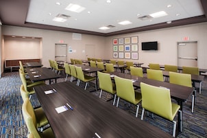 Uma sala de conferências com várias mesas e cadeiras, uma televisão de tela plana fixada na parede e um sinal de saída.
