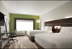 Quarto de hotel com duas camas, uma escrivaninha, uma cadeira, televisão e uma janela grande.