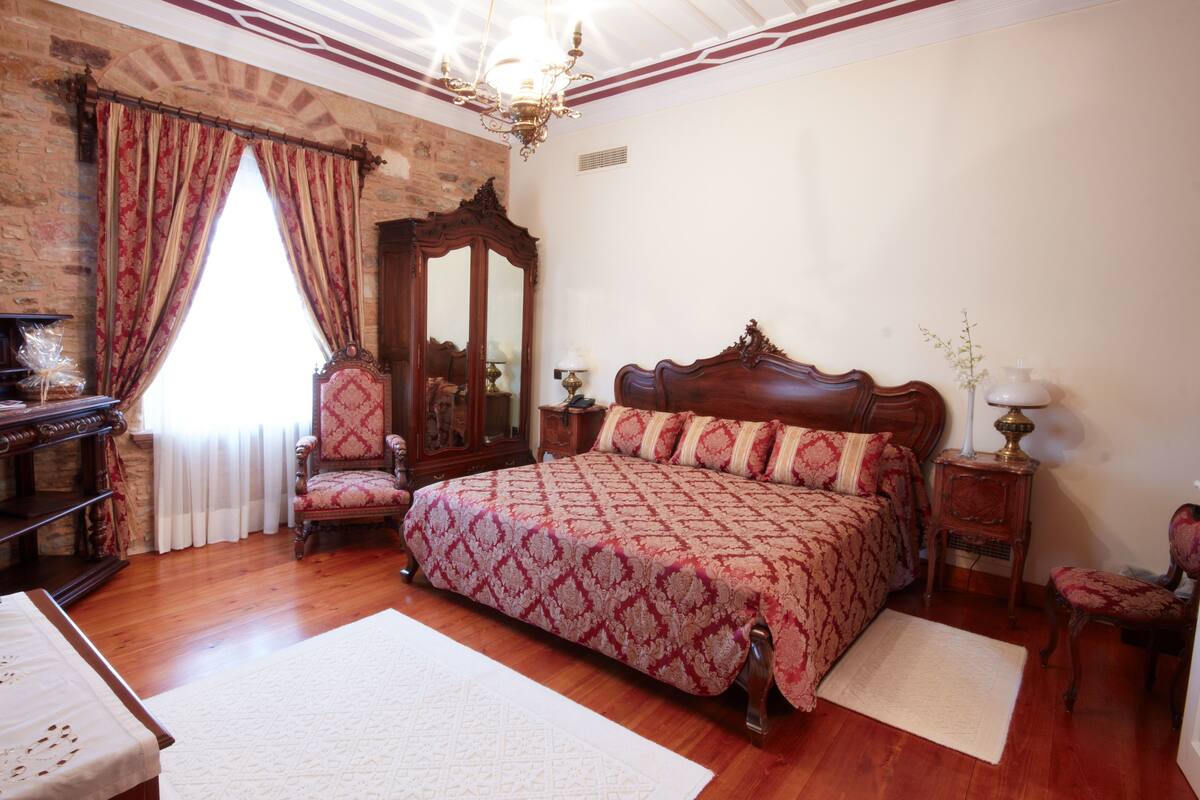 Quarto com cama grande, cabeceira de madeira, espelho, cômoda e lustre.